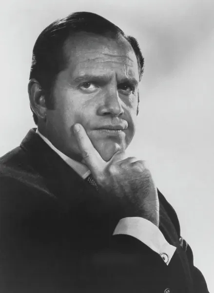 Portrait Of American Comedian Alan King Posing In Front Of A Curtain